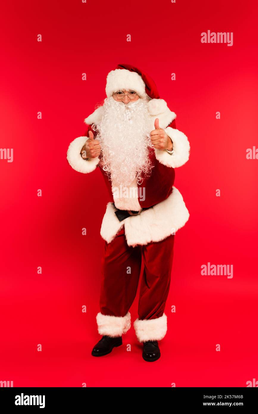 Santa claus in eyeglasses showing like gesture at camera on red ...