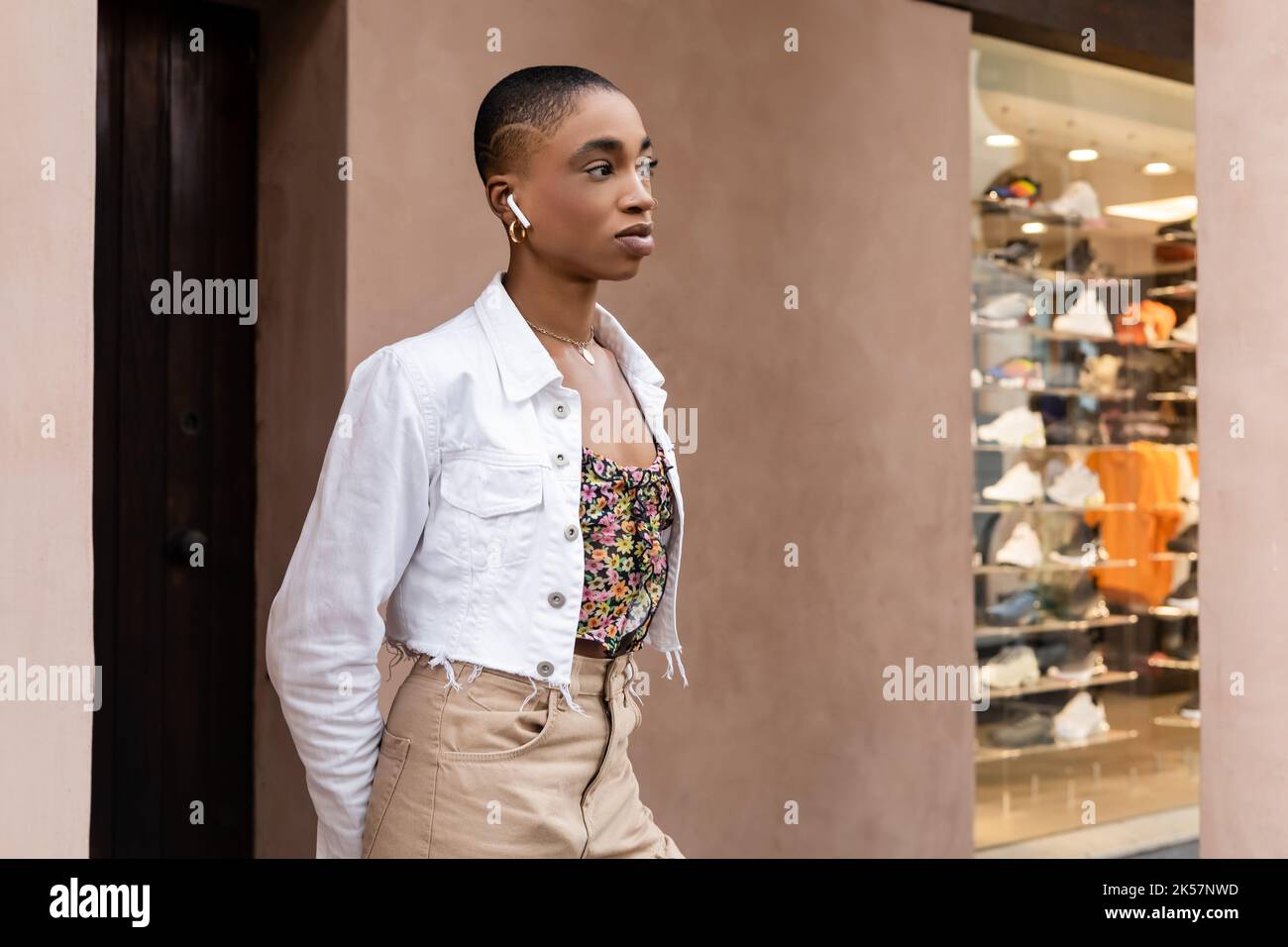 Trendy african american woman in earphone standing near building on ...
