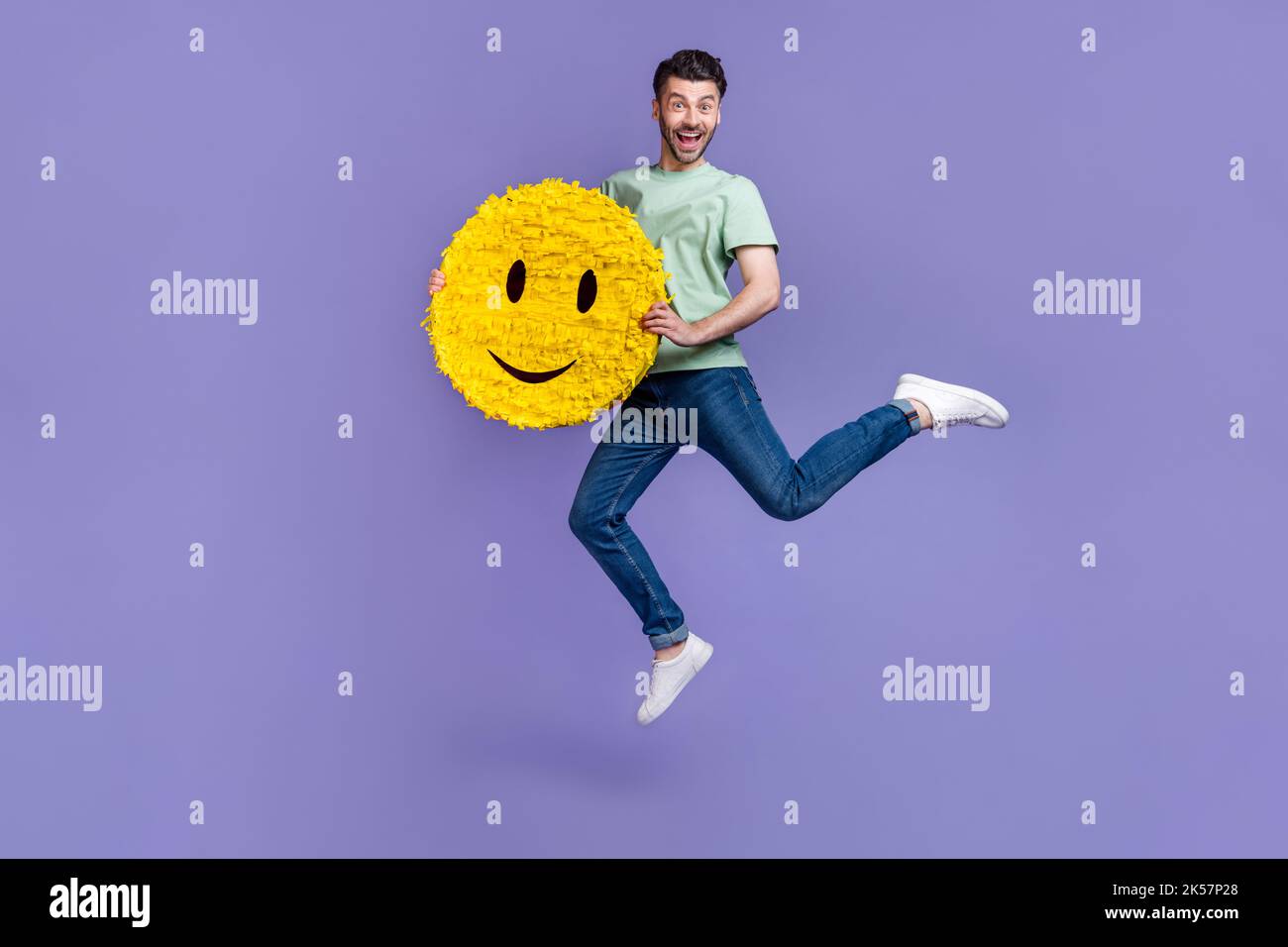 Full body photo of attractive young guy jump holding smile emoji pinata ...