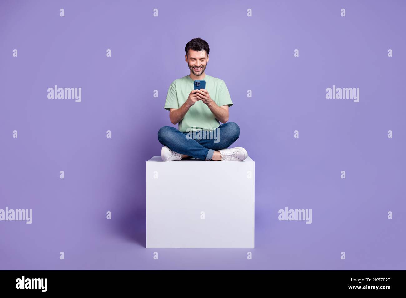 Full body photo of attractive young guy hold gadget sit white cube ...