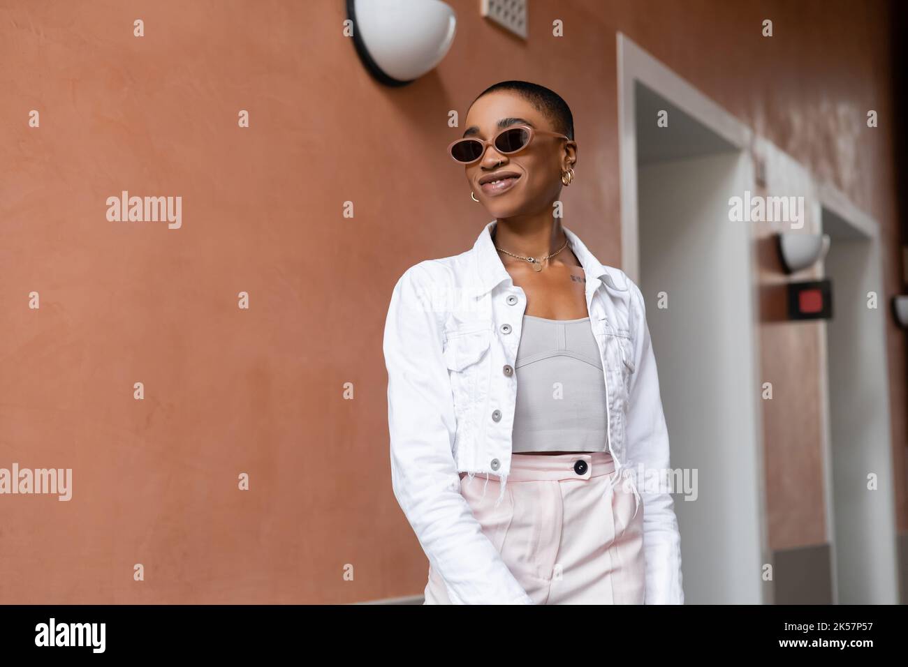Smiling african american woman in sunglasses and white jacket standing ...
