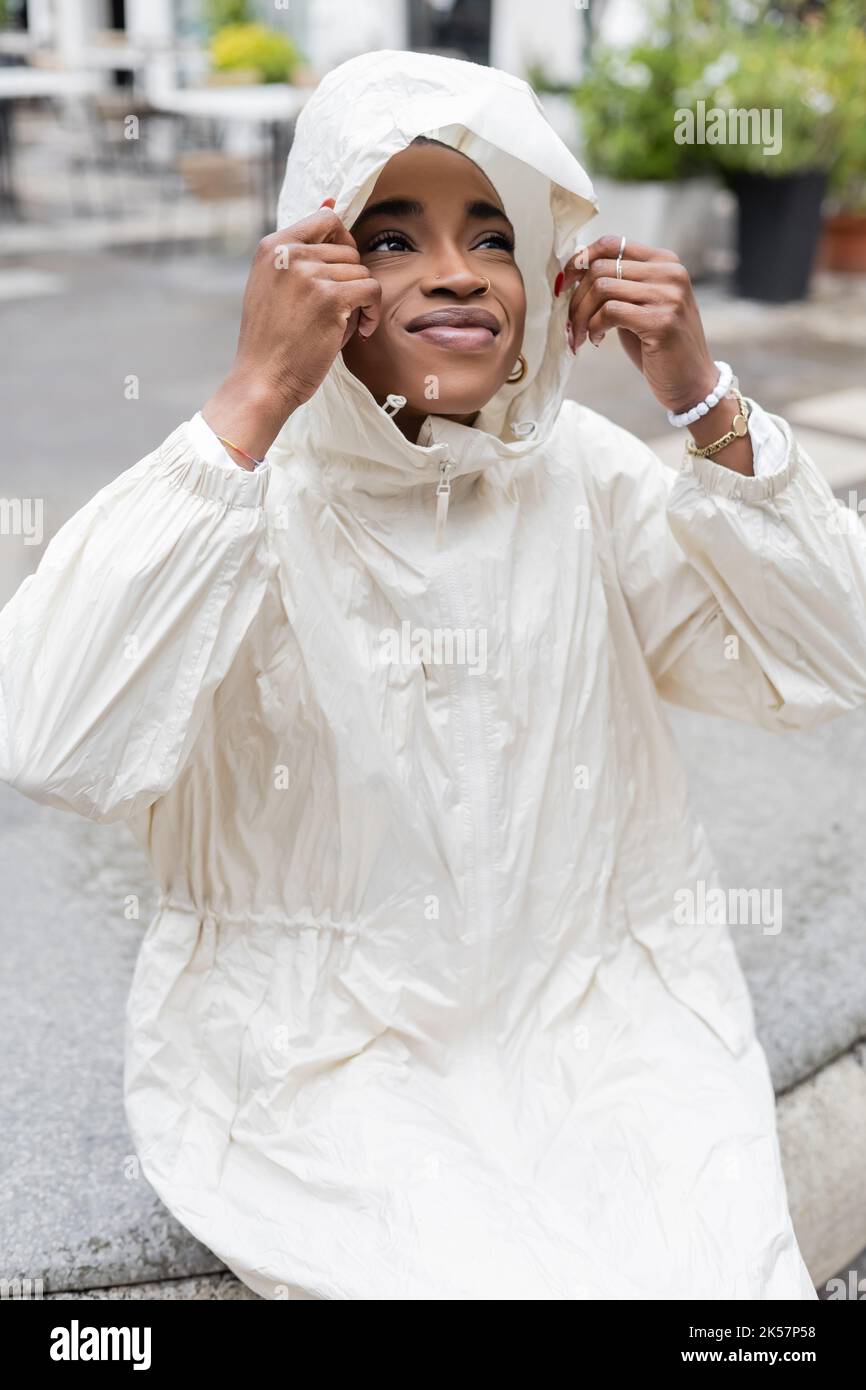 Fashionable african american woman in raincoat looking away on urban ...