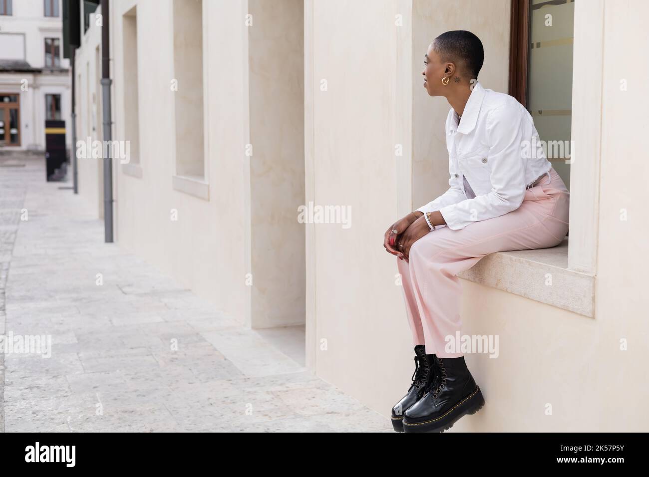 Side view of stylish african american woman sitting on windowsill of ...