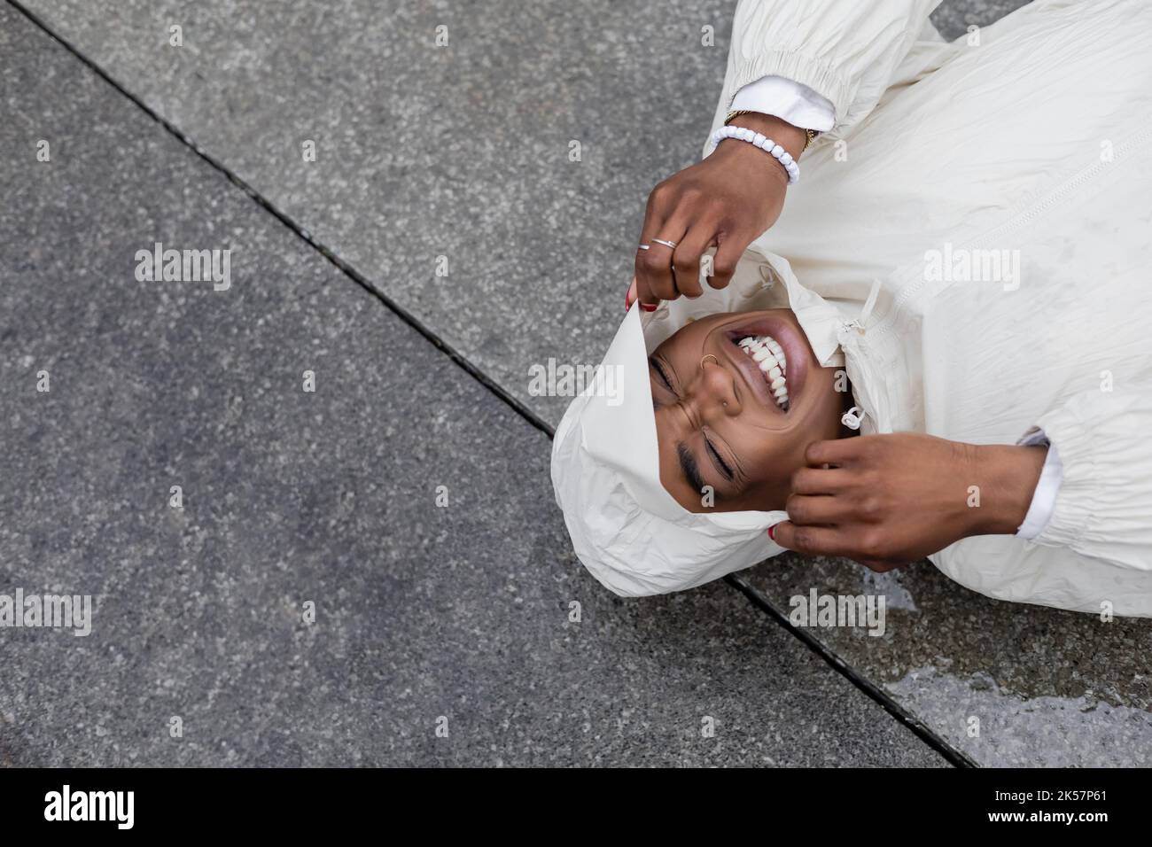 Top view of cheerful african american woman in raincoat lying on urban ...