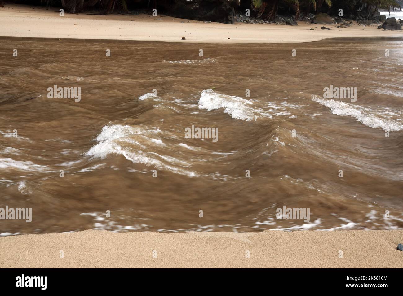 rivermouth on sandy beach on a rising tide, with waves running up river ...