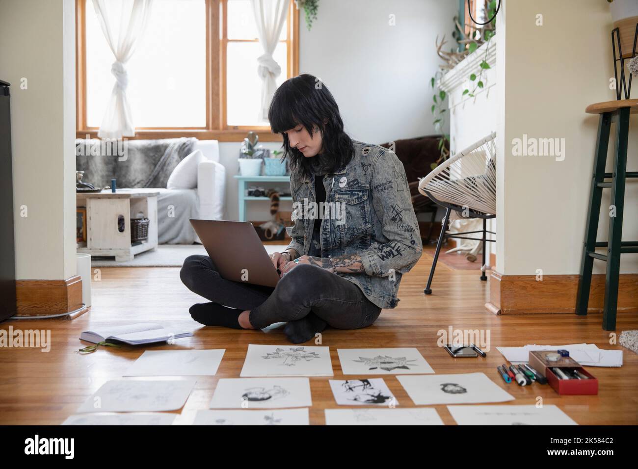 Young female transgender artist with laptop and drawings on floor Stock ...