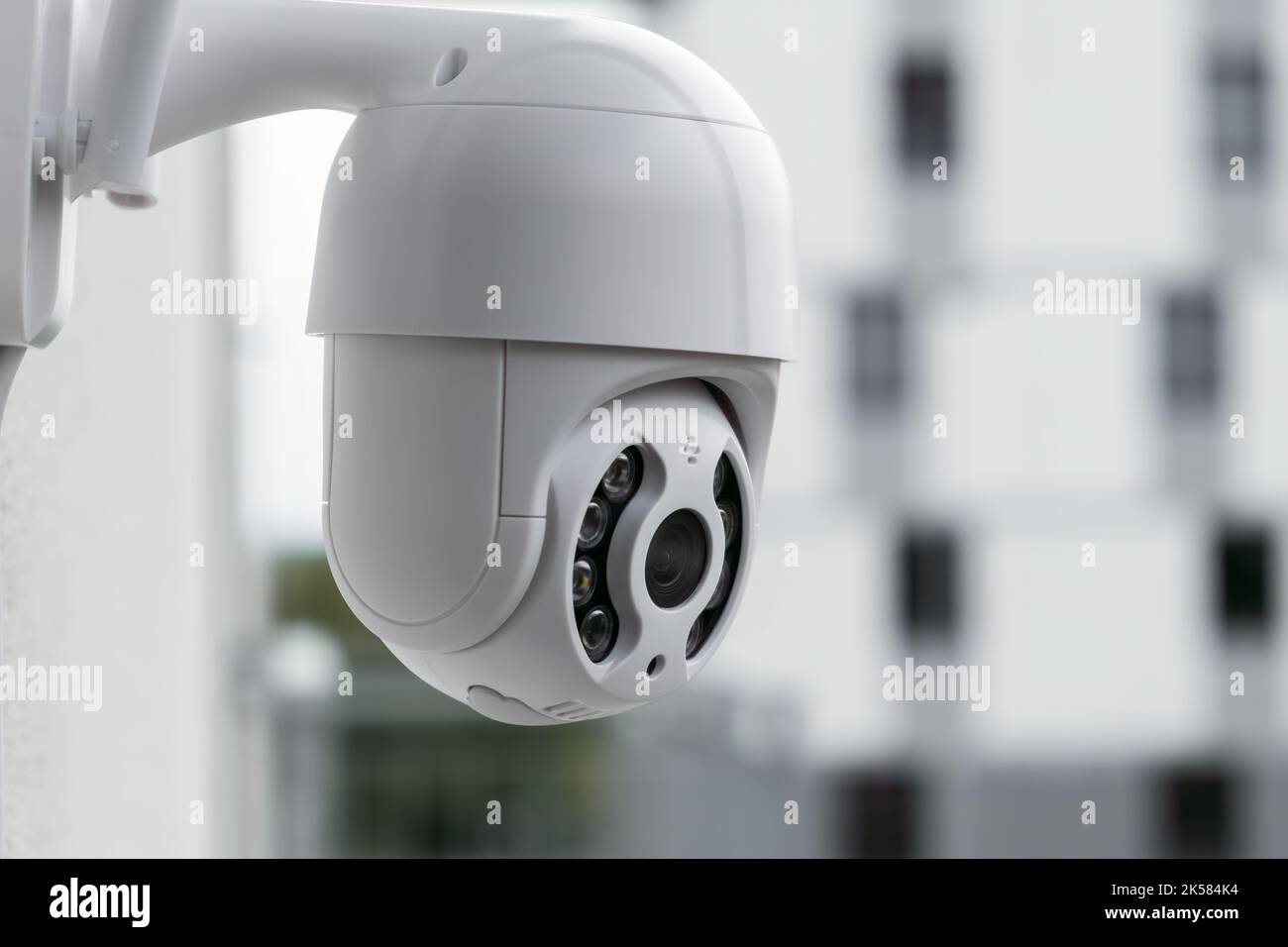 Modern CCTV camera on a wall with a blurred multi-storey building on ...