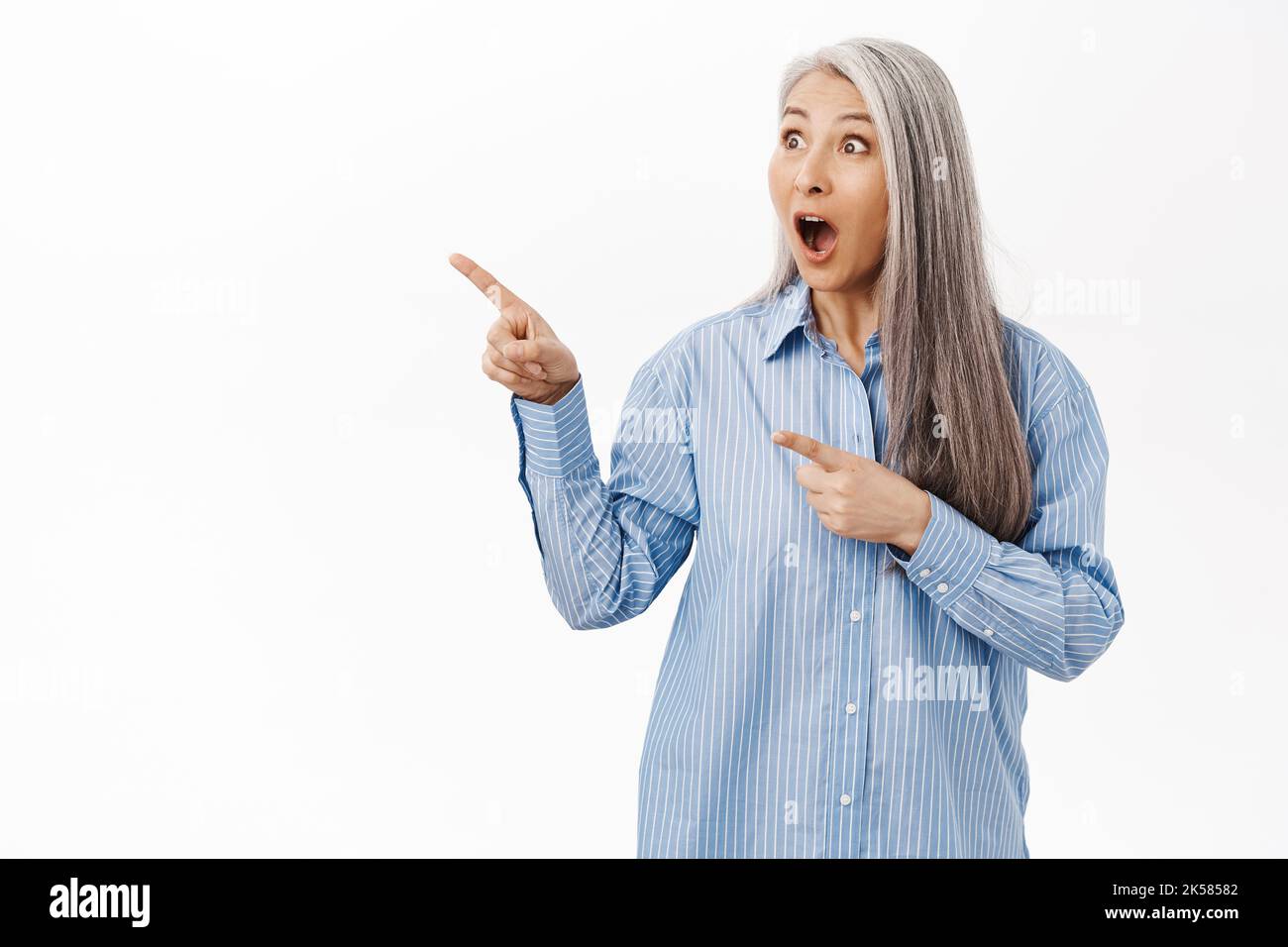 Portrait of amazed senior woman, asian female model pointing finger ...