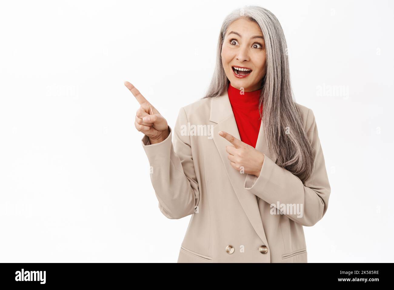 Excited asian businesswoman in suit pointing finger left and looking ...