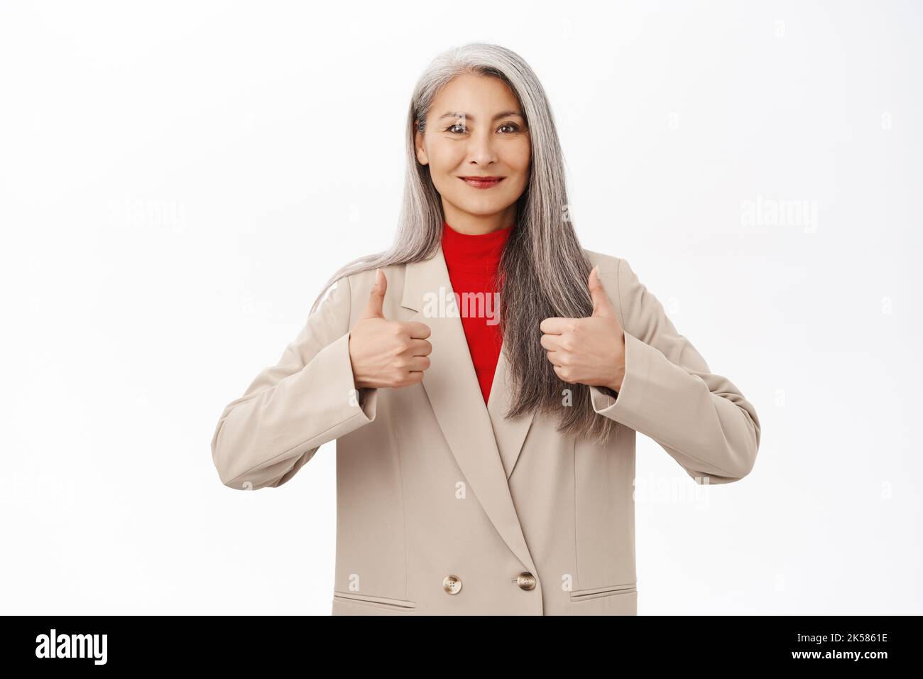 Smiling old asian lady in business suit, showing thumbs up in approval ...