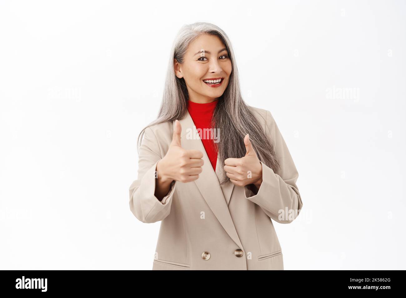Smiling old asian lady in business suit, showing thumbs up in approval ...