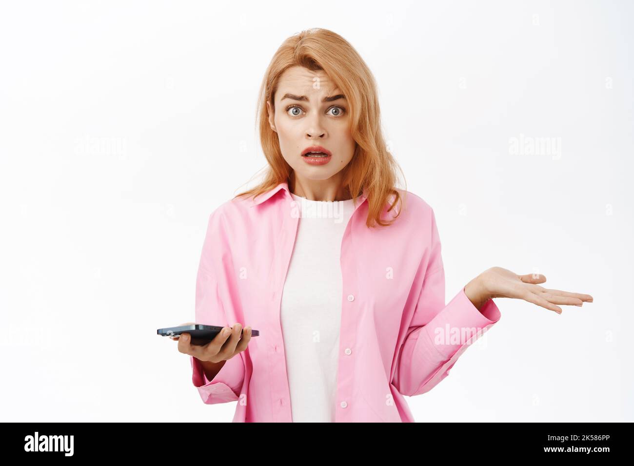 Confused young woman looking puzzled and using mobile phone, holding ...