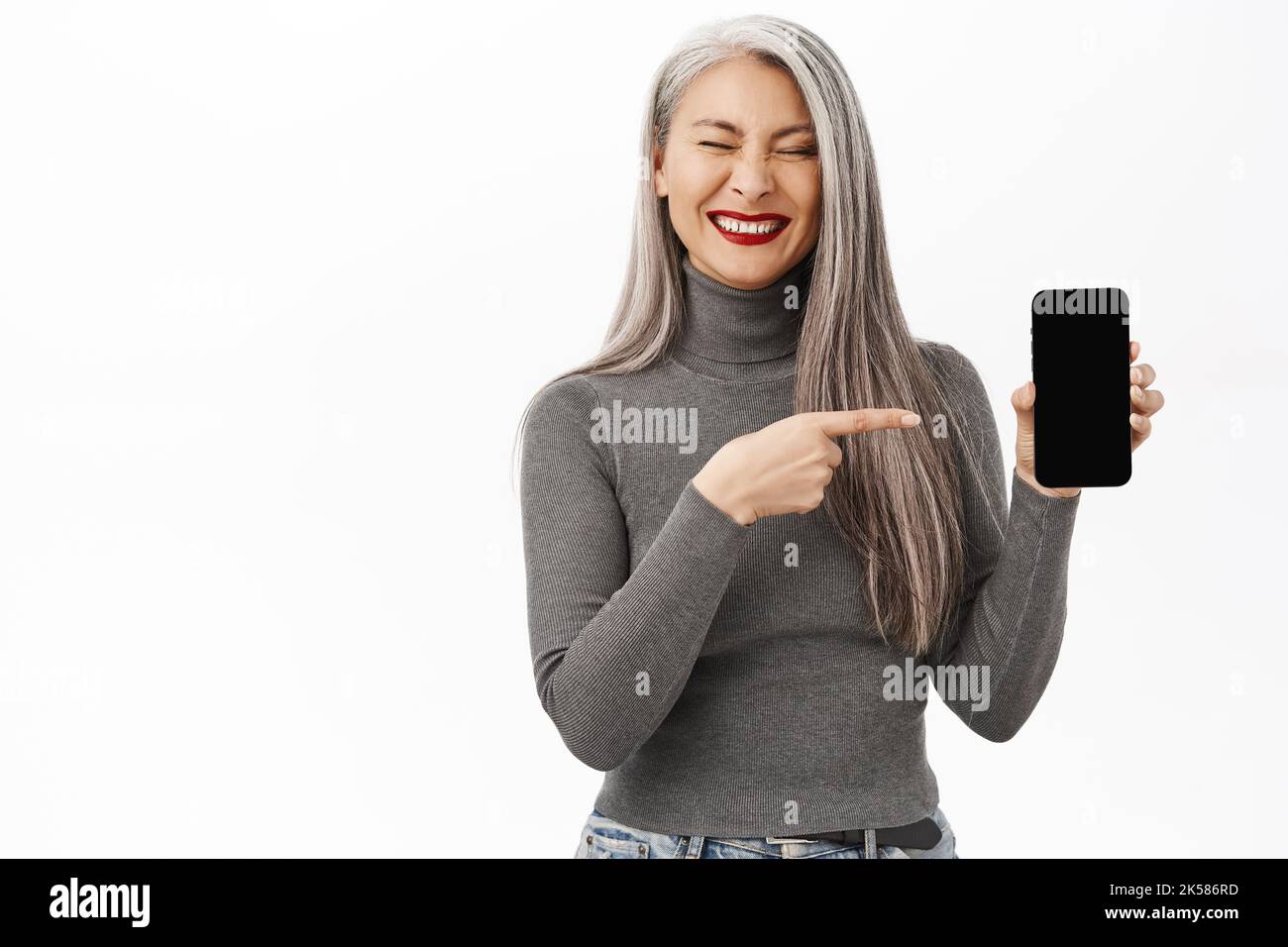 Portrait of happy asian middle aged woman laughing and smiling, pointing at smth funny on ...
