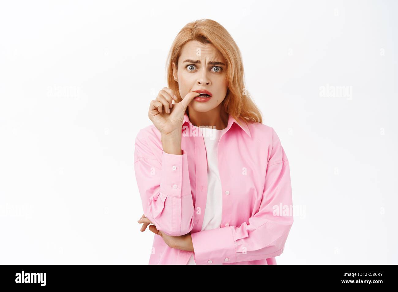 Scared and anxious young woman biting finger, looking worried at camera ...