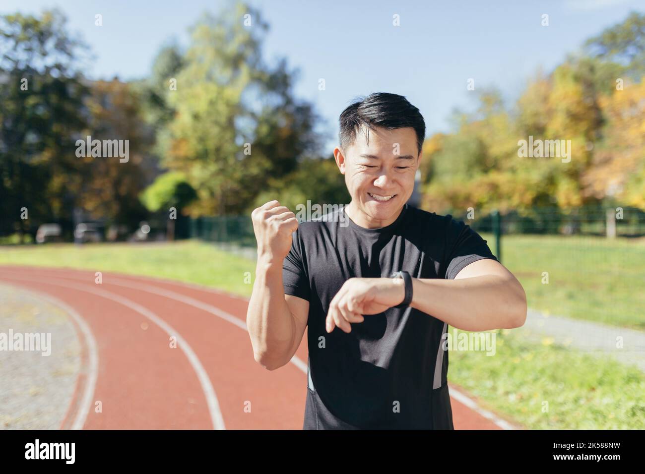 Asian running in the stadium sunny day man looks at the smartwatch and ...