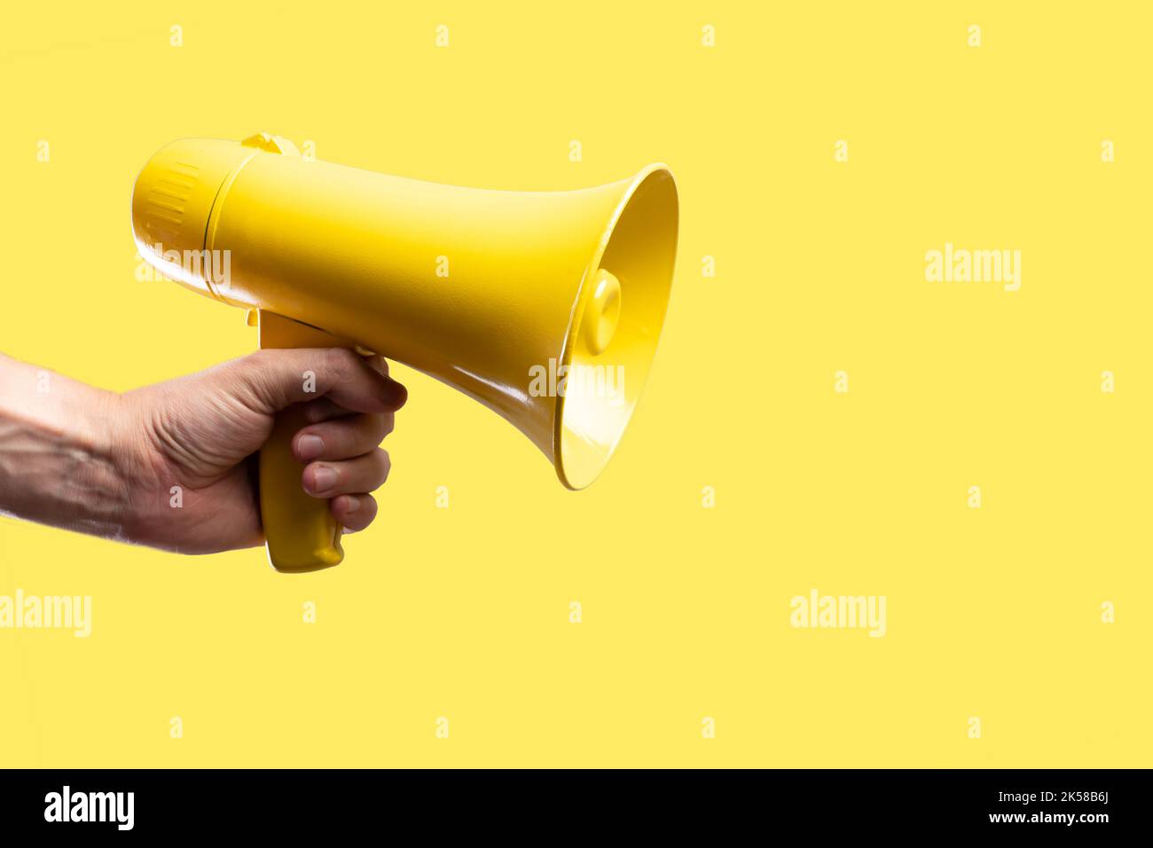 On a yellow background, a yellow megaphone in a person's hand. Symbol ...