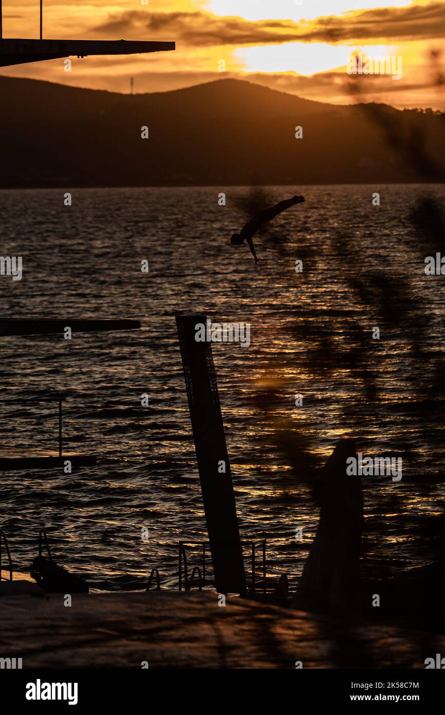 Boy jumps off the diving platform into the Adriatic Sea during sunset ...