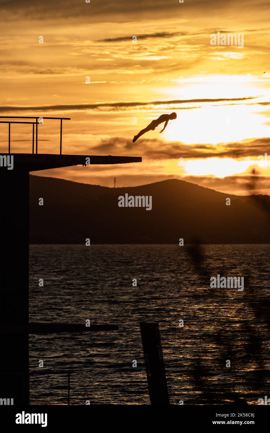 Boy jumps off the diving platform into the Adriatic Sea during sunset ...