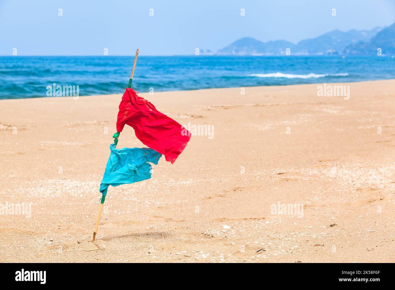 Red and blue signal flags pinned on beach sand at sunny coast (copy ...
