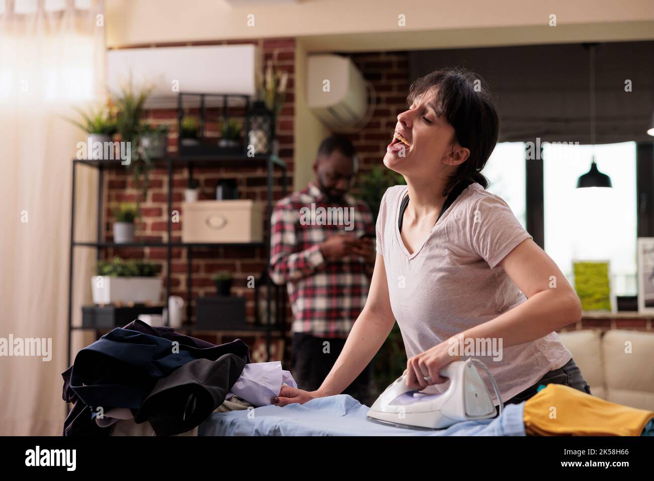 Happy smiling woman singing and ironing clothes on board, husband on ...
