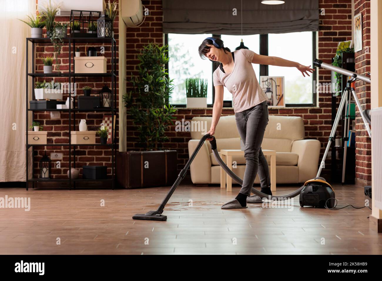 Positive woman doing spring cleaning at home, singing while vacuuming ...
