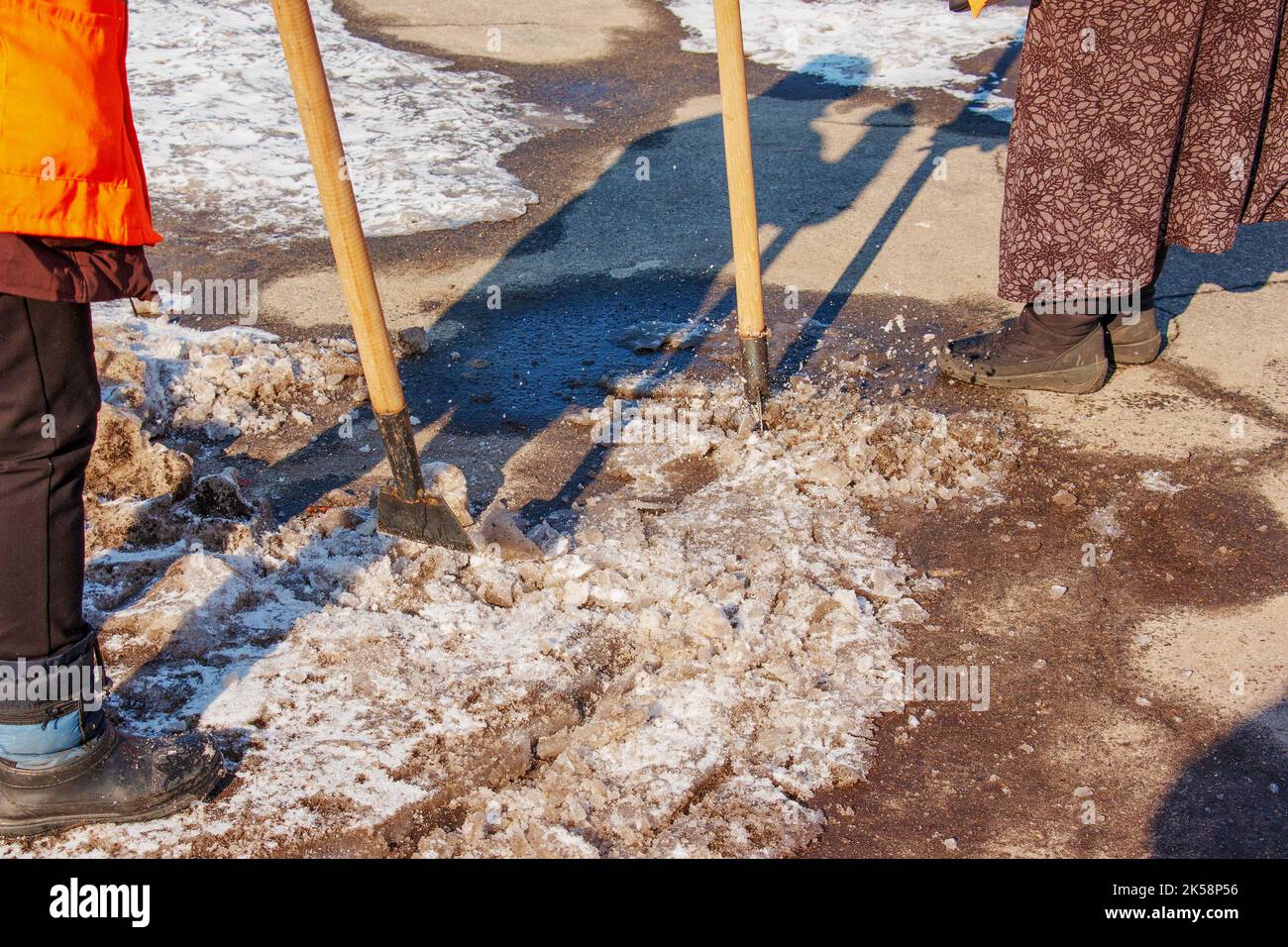 A woman worker cleans the ice and removes snow from paving slabs using ...