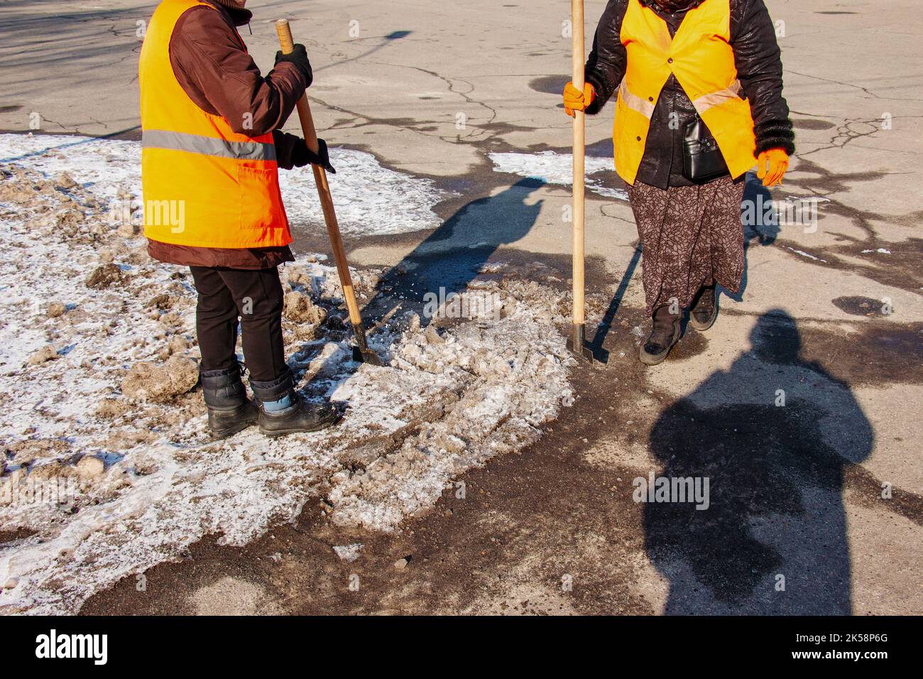 A woman worker cleans the ice and removes snow from paving slabs using ...