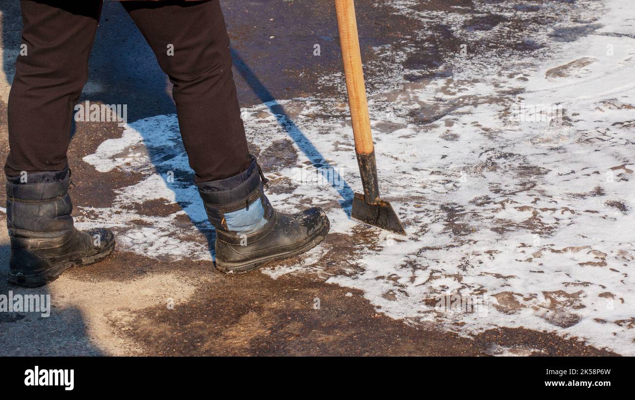 A woman worker cleans the ice and removes snow from paving slabs using ...