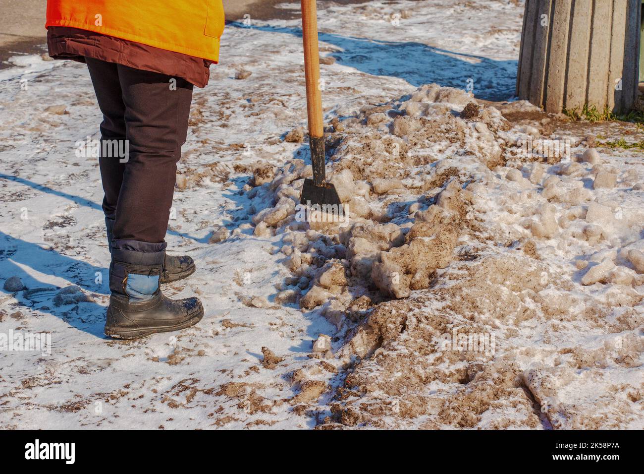 A woman worker cleans the ice and removes snow from paving slabs using ...
