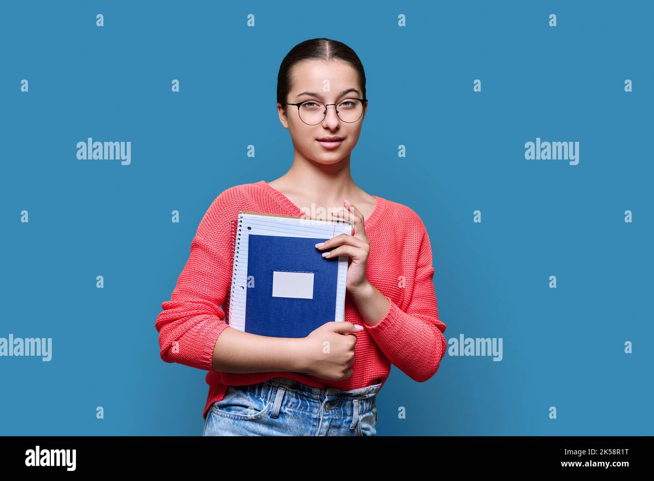 Portrait of teenage female student holding notebooks looking at camera ...