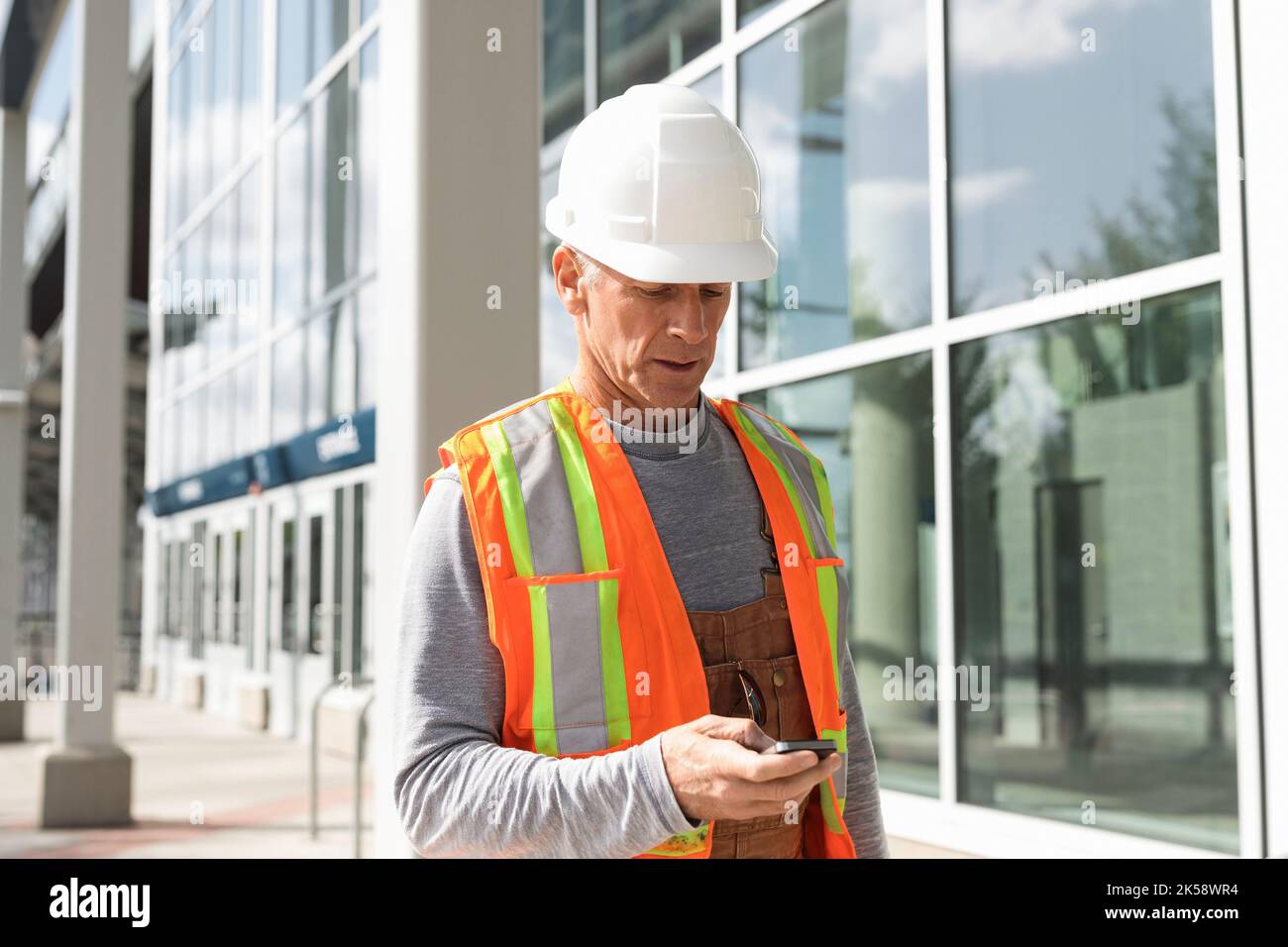 Construction worker using smartphone outside building Stock Photo - Alamy