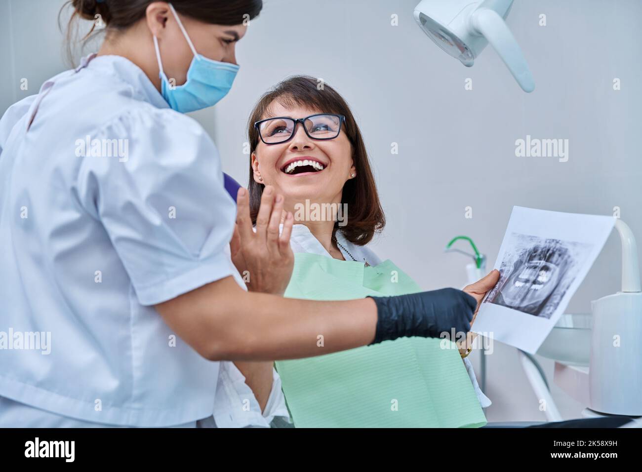 Female dentist talking to woman patient, discussing x-rays of teeth and ...