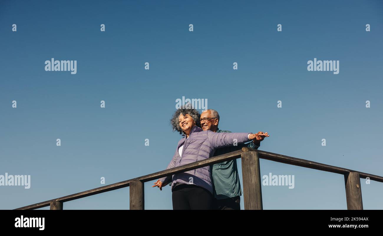Cheerful senior couple smiling and spreading their arms while standing ...