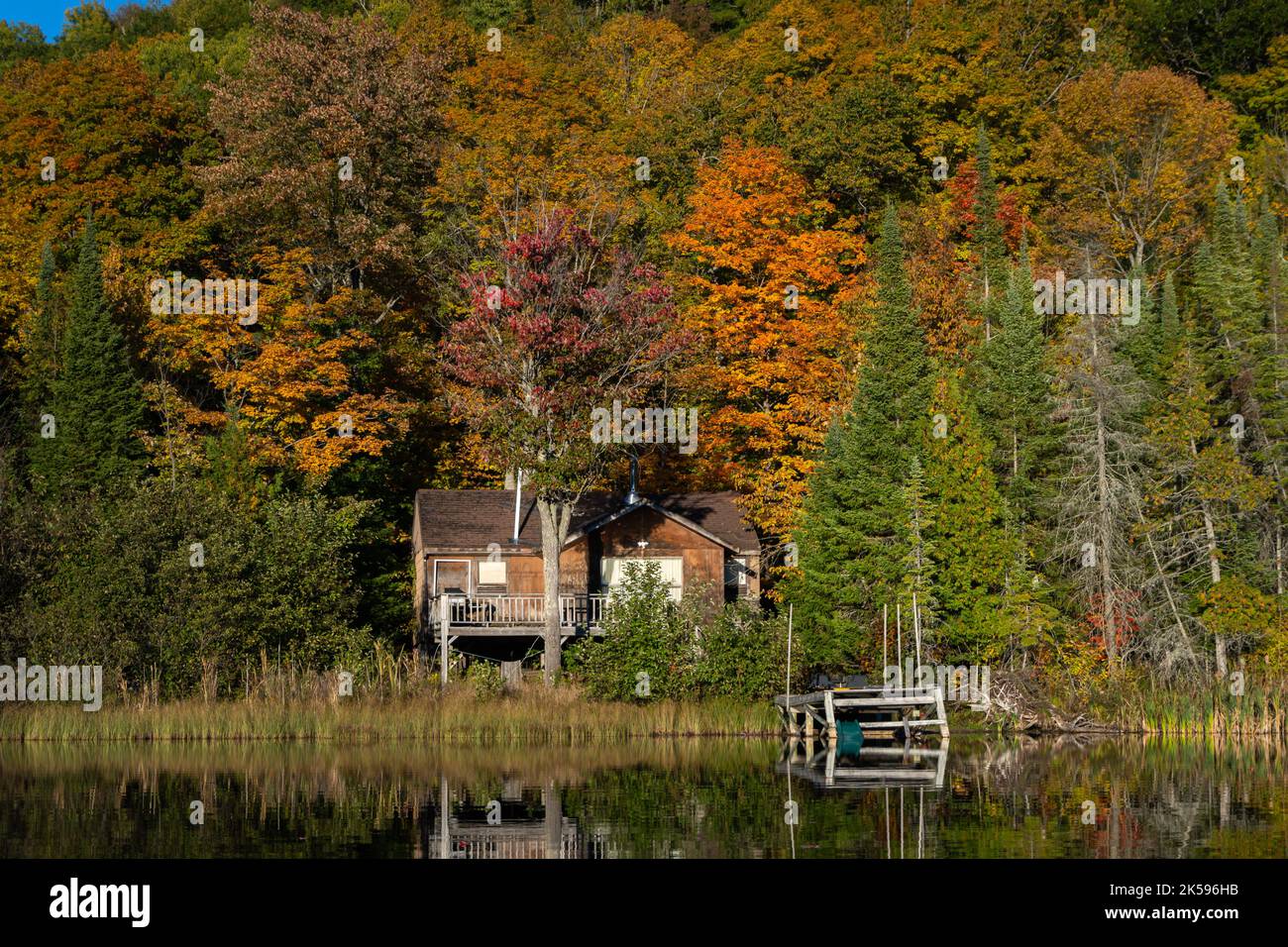 An old cabin sits nestled between a lake and the colourful fall foliage ...