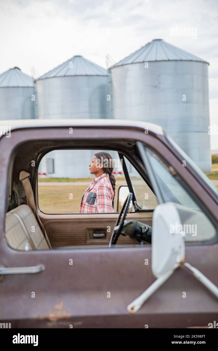 Thoughtful, confident female farmer standing outside pickup truck on ...