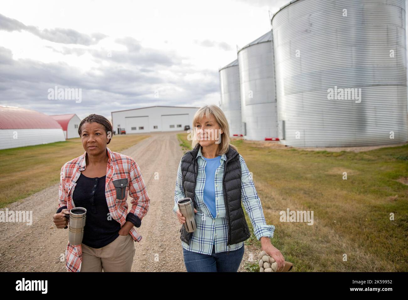 Female farmers drinking coffee and walking along silos on farm Stock ...