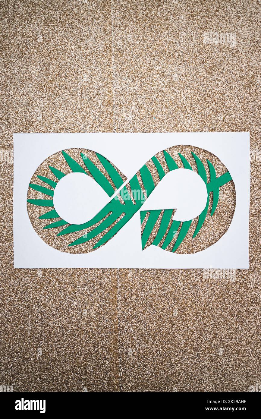 circular economy symbol on paper cutout with tropical leaf underneath ...