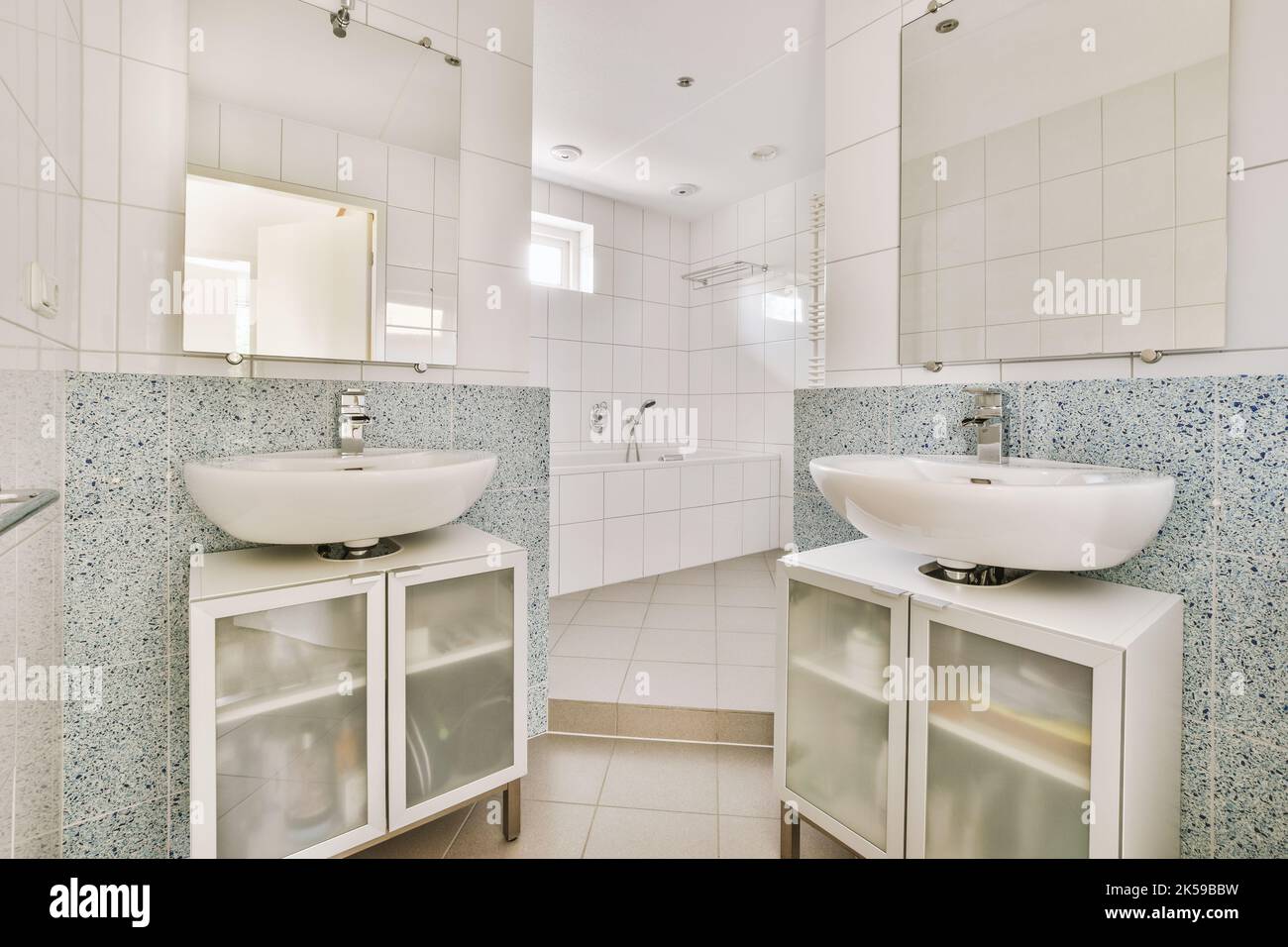 Flush toilet located between sink and shower in small tiled bathroom of ...