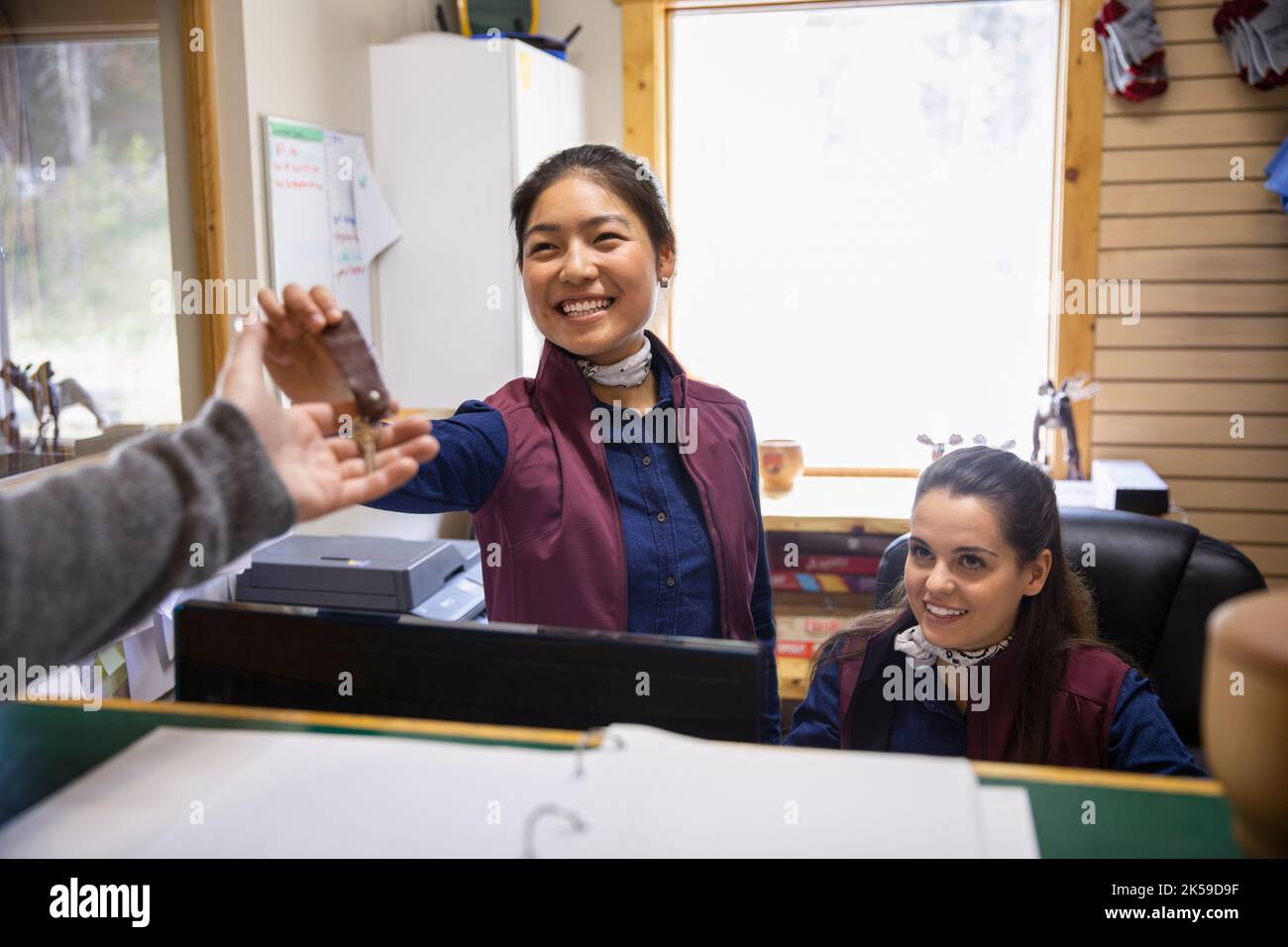 Smiling, friendly female hotel receptionist giving room key to guest at ...