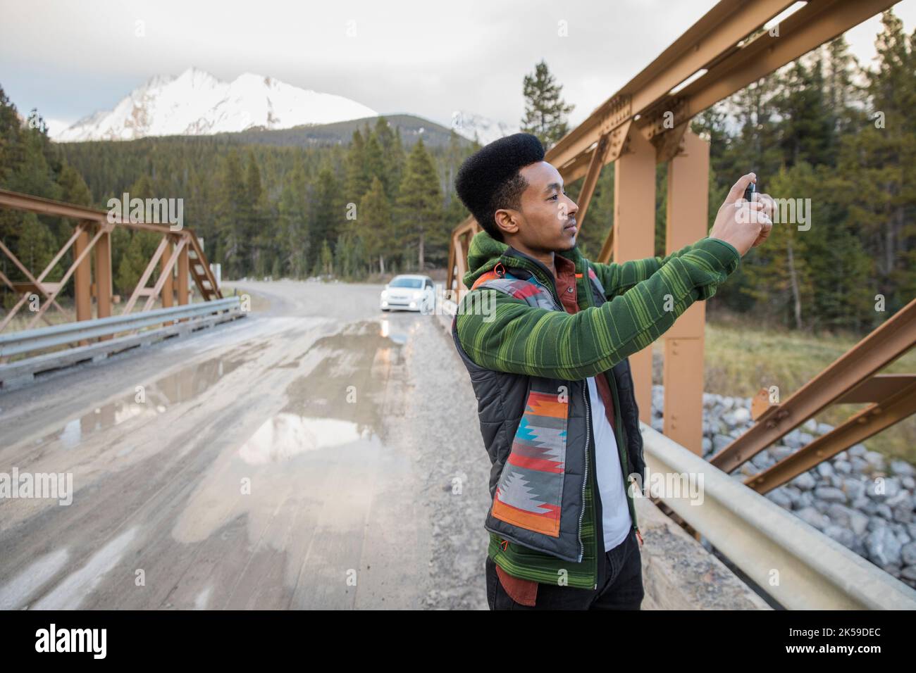 Young man using camera phone on remote bridge Stock Photo - Alamy