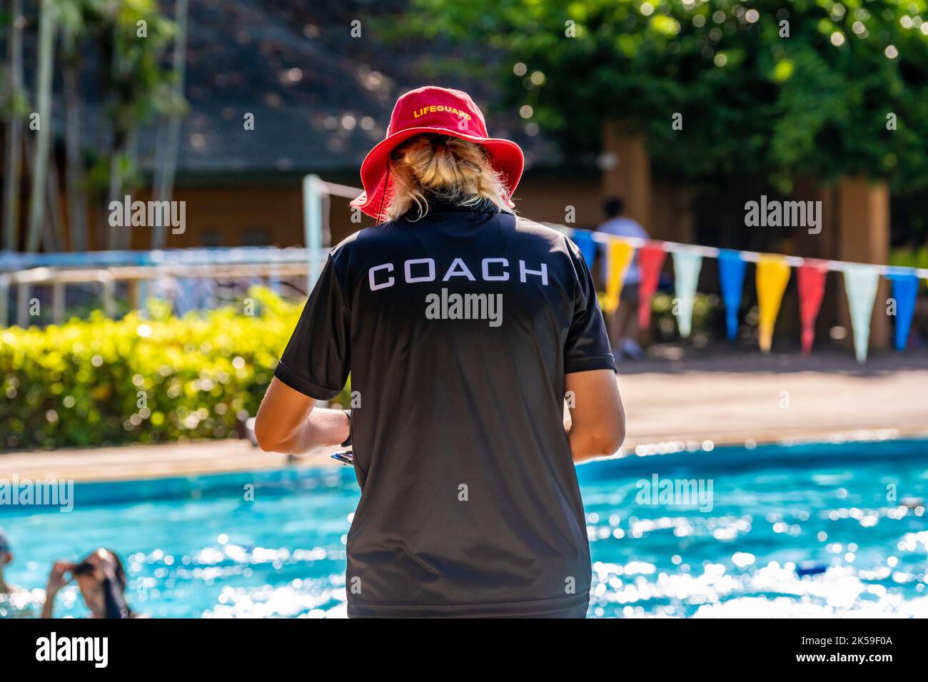 Back View Of Swimming Coaches Wearing Coach Shirt Working At An
