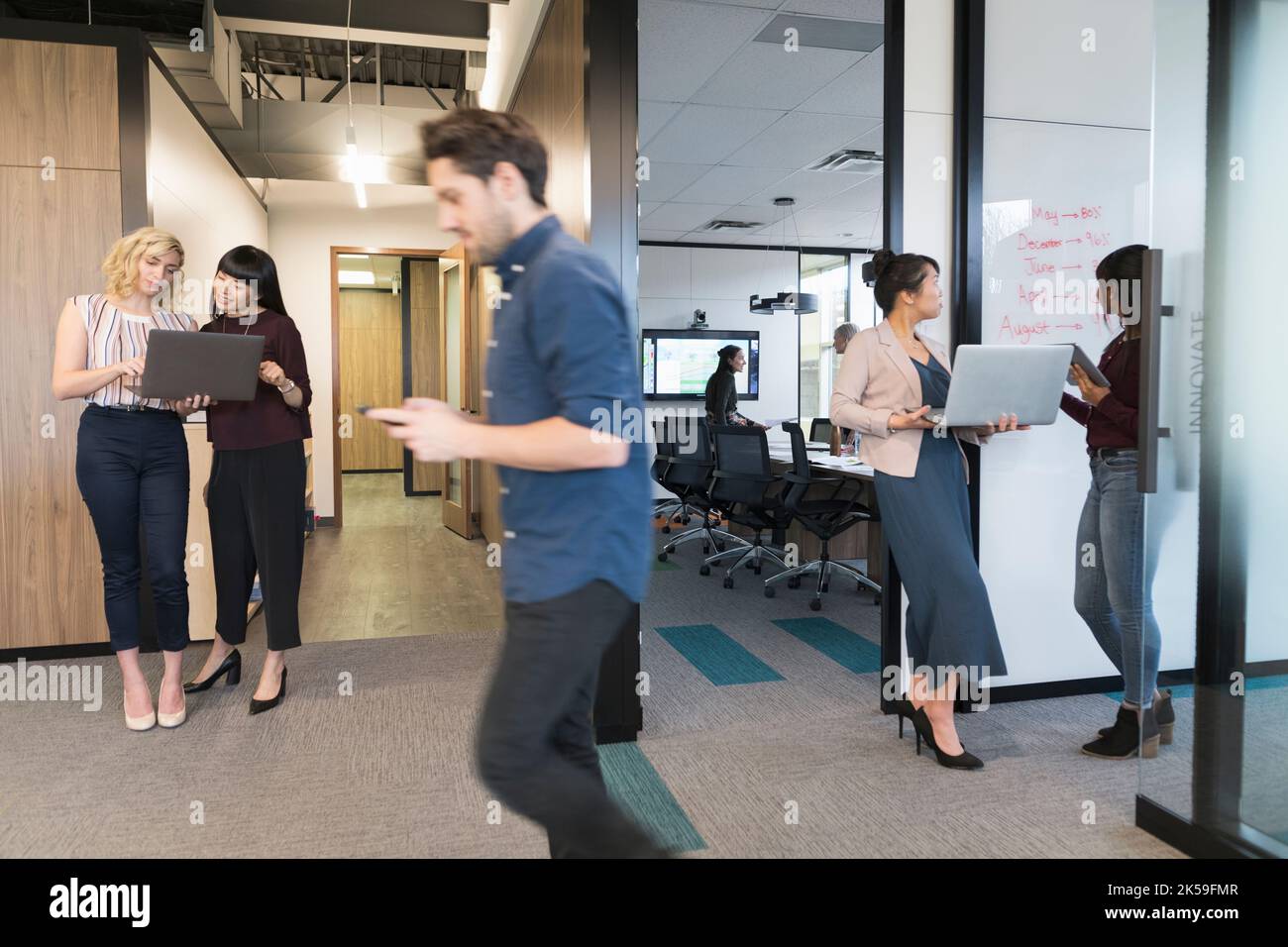 colleagues working in modern office corridor with man walking past ...