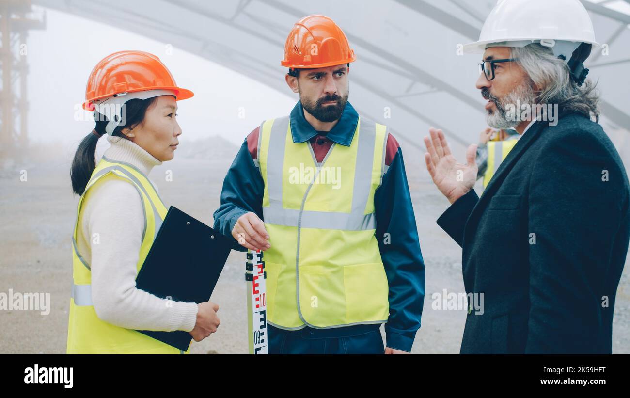 Builders wearing uniform are talking at construction site while ...