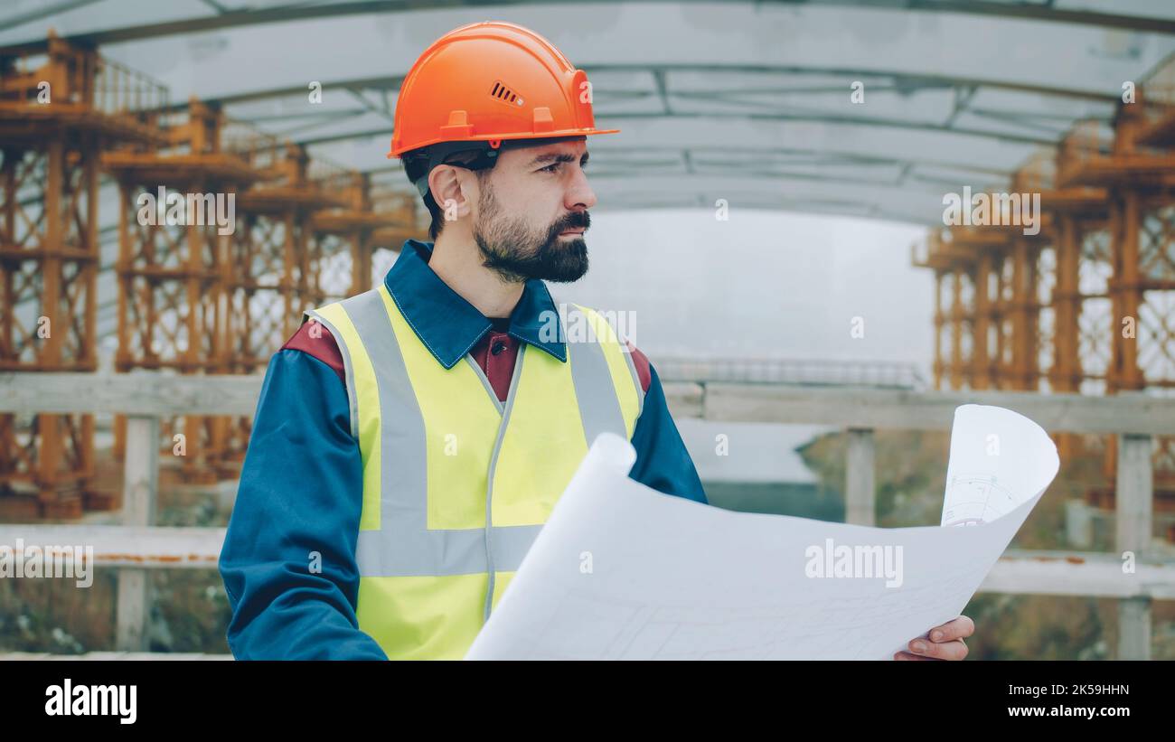 Portrait of serious foreman wearing uniform checking blueprint and ...