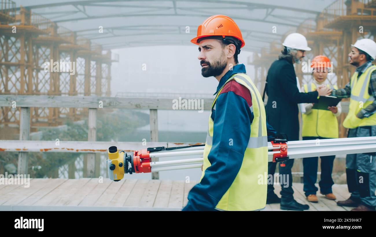 serious male surveyor in uniform walking in construction site holding ...