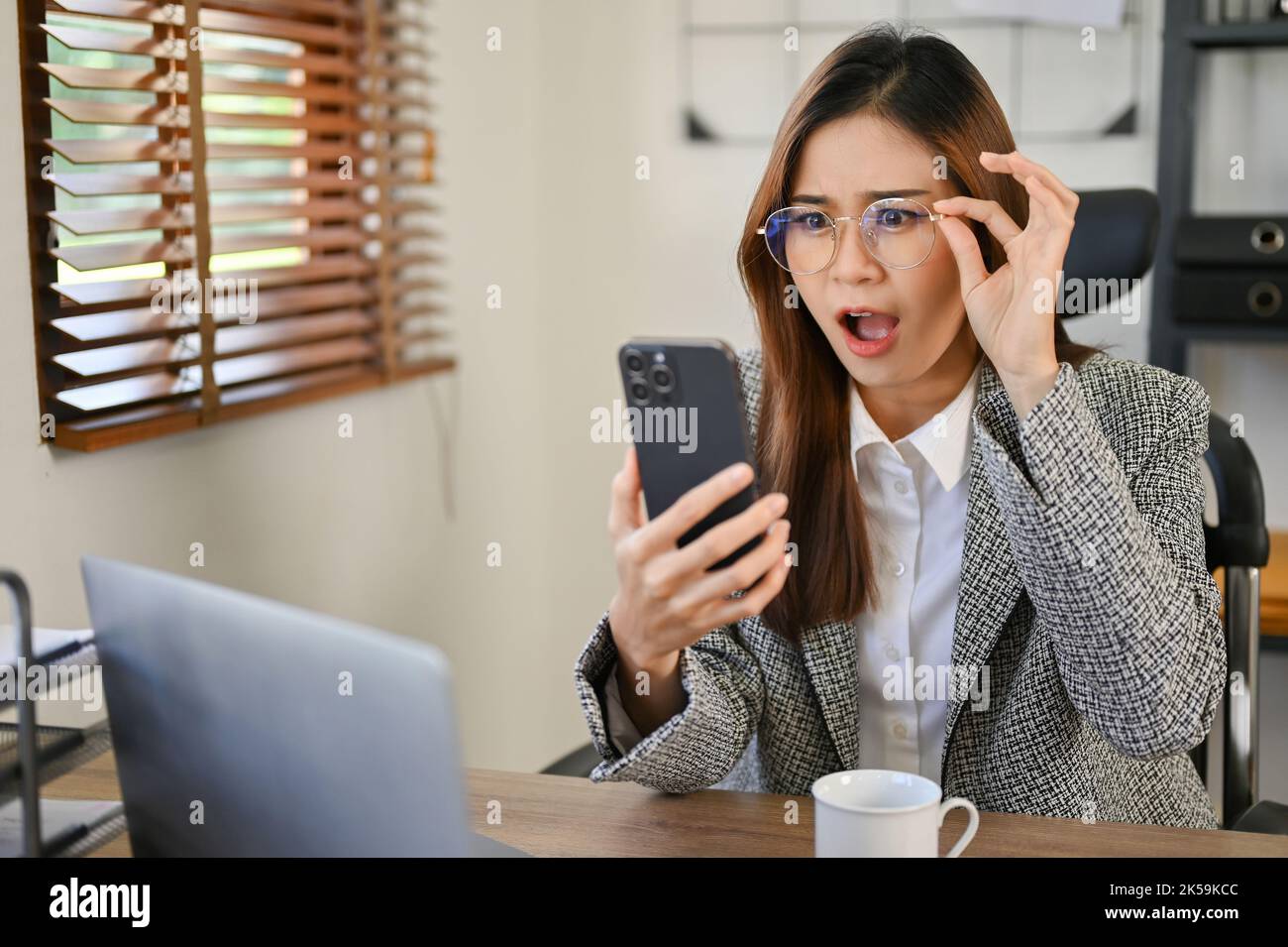Surprised and shocked young Asian businesswoman or female boss sitting ...