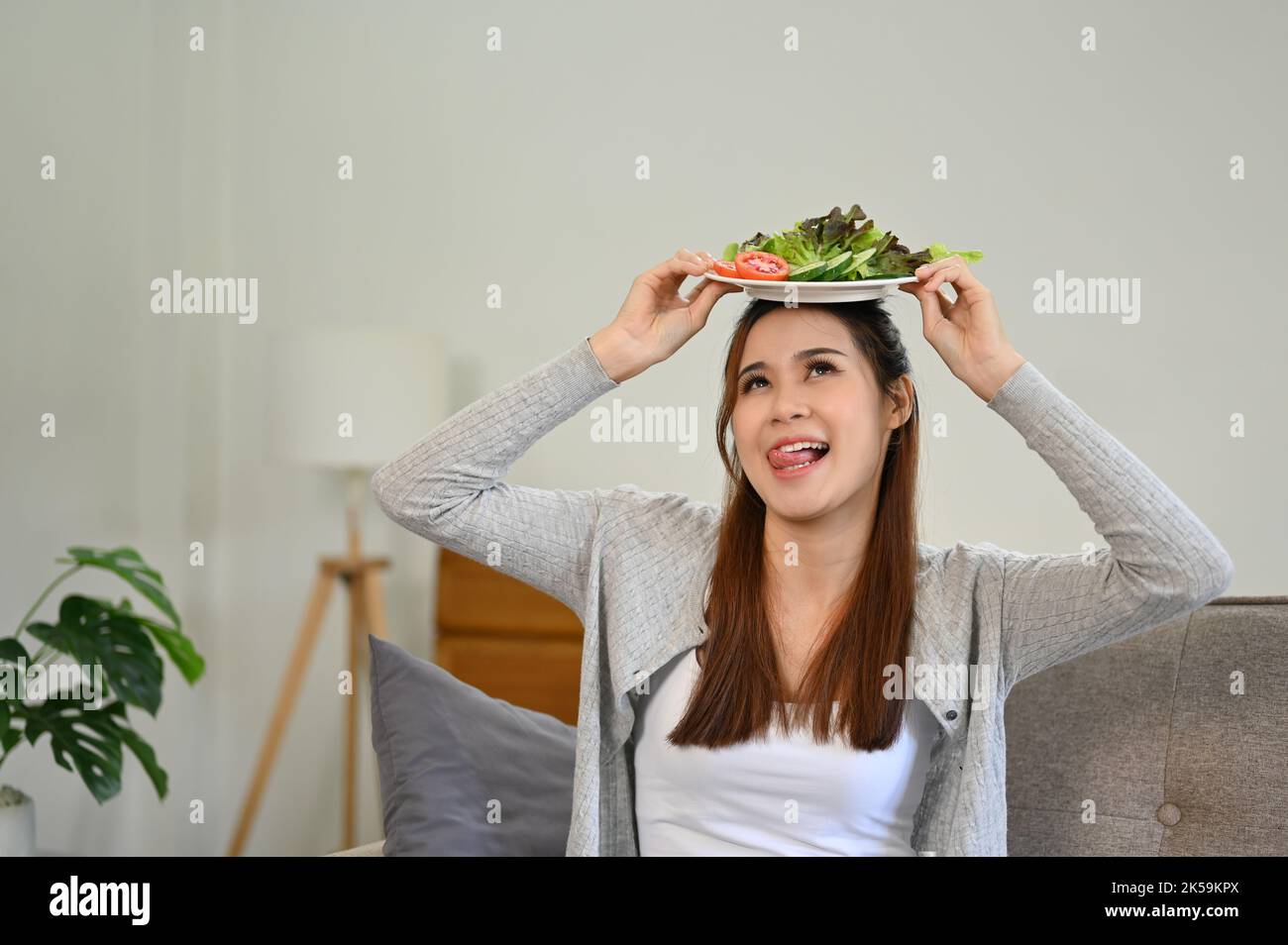 Pretty and joyful young Asian female putting a plate of her green salad ...
