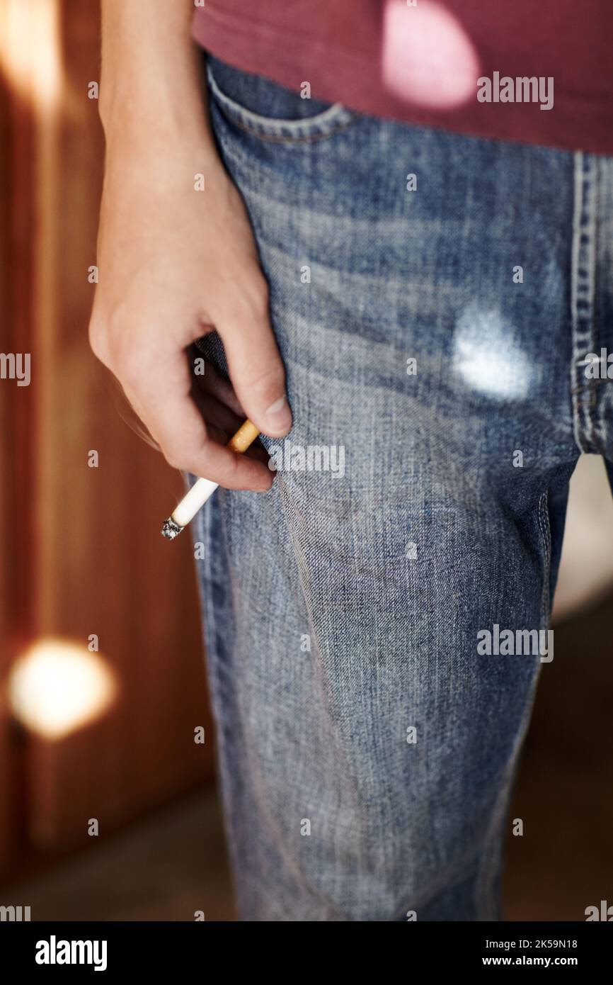 Teen temptation. Closeup of a persons hand holding a burning cigarette ...