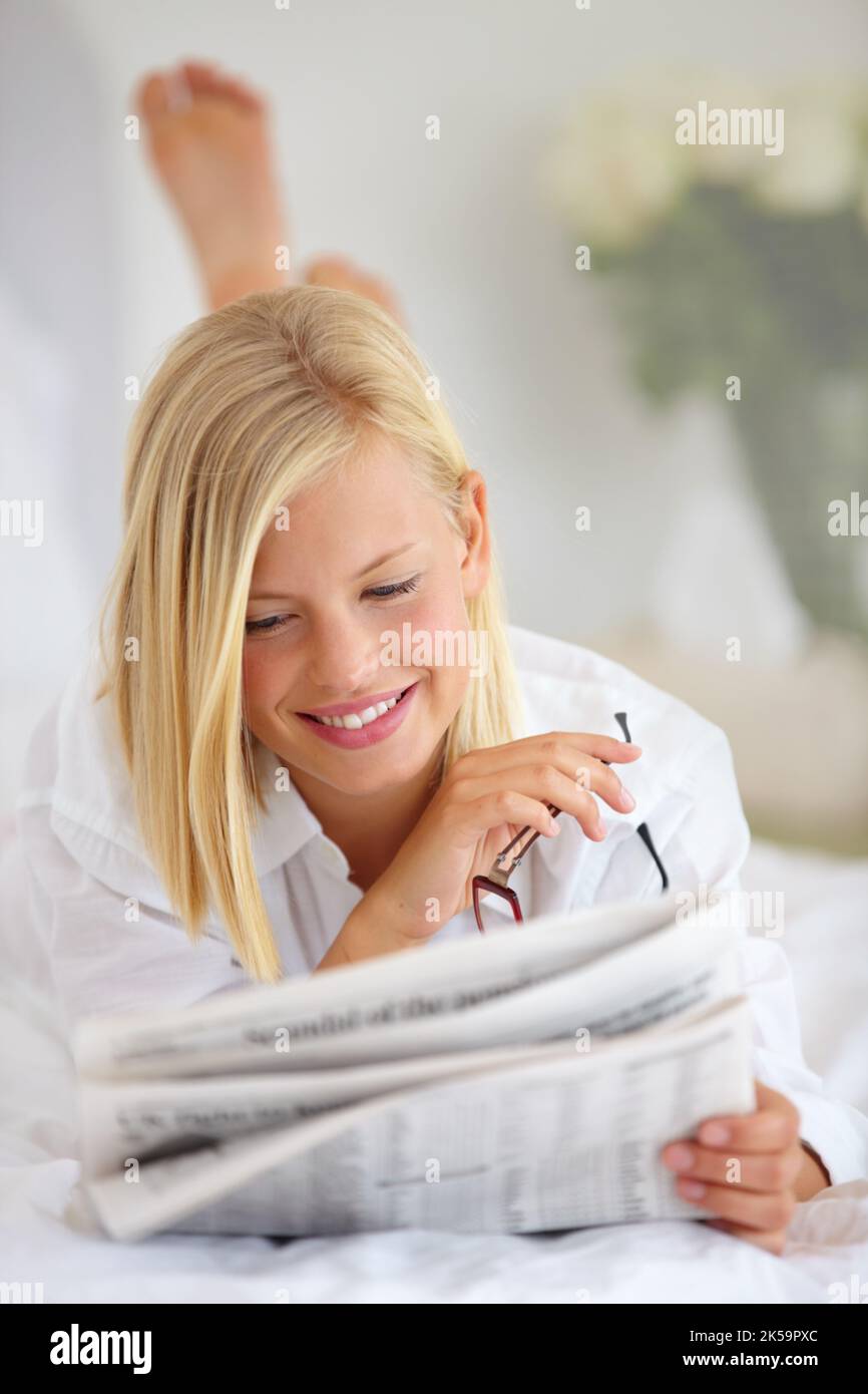 Getting her daily news feed. Young woman lying on the bed at home and reading the newspaper ...