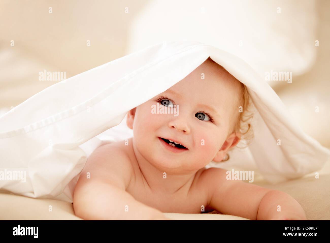 Filled curiousity. Cute baby boy lying under a sheet playfully and ...